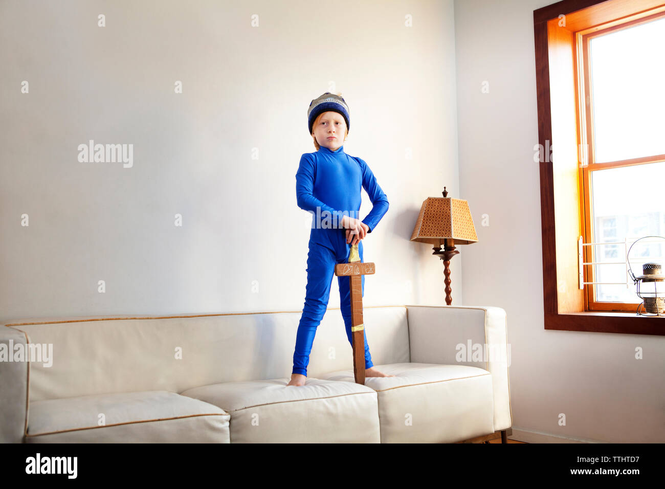 Boy in superhero costume holding sword while standing on sofa Stock ...