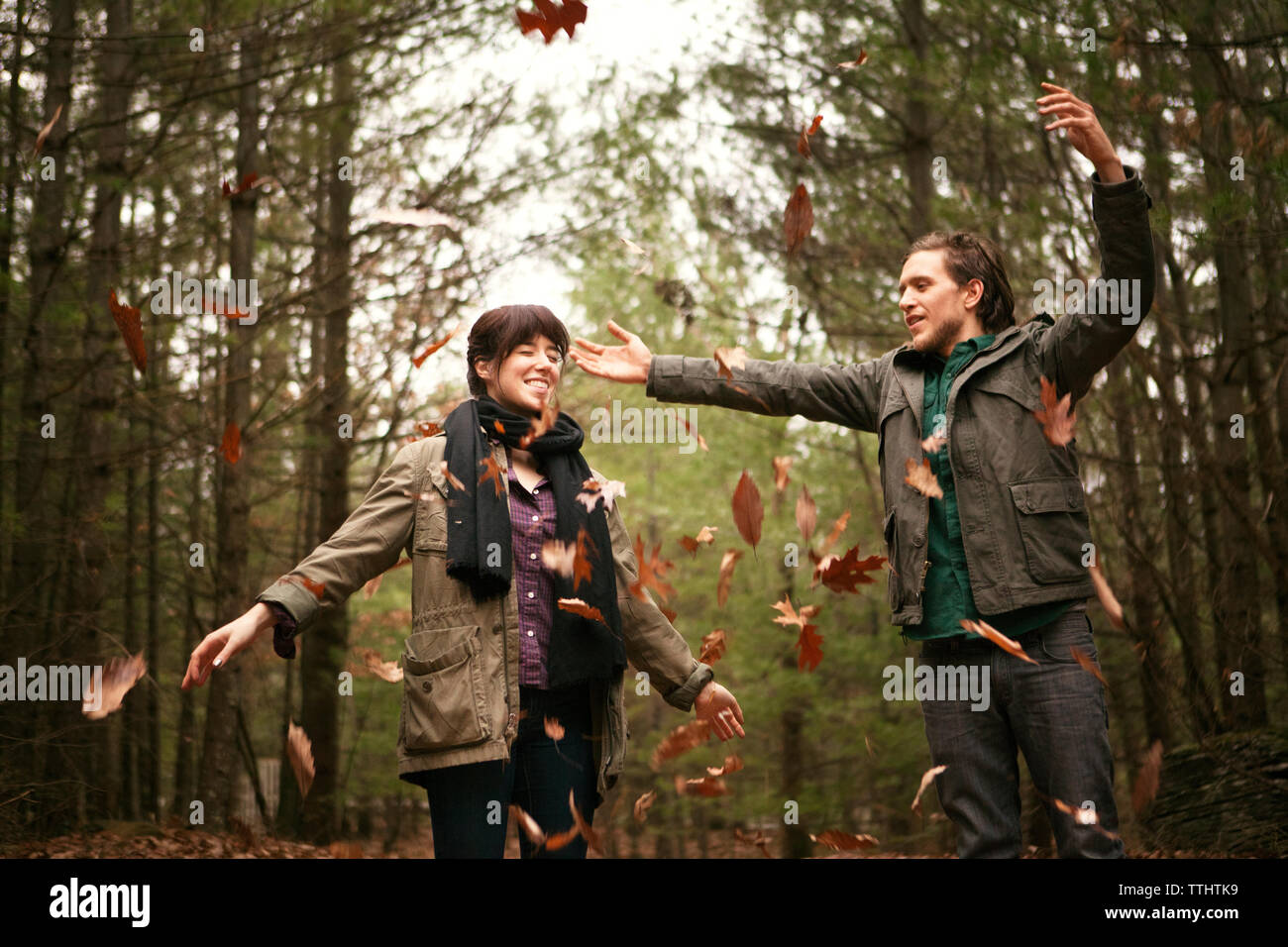 Playful couple throwing leaves while standing in forest Stock Photo - Alamy