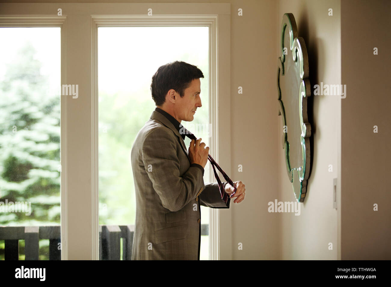 Side view of man adjusting tie while looking at mirror Stock Photo - Alamy