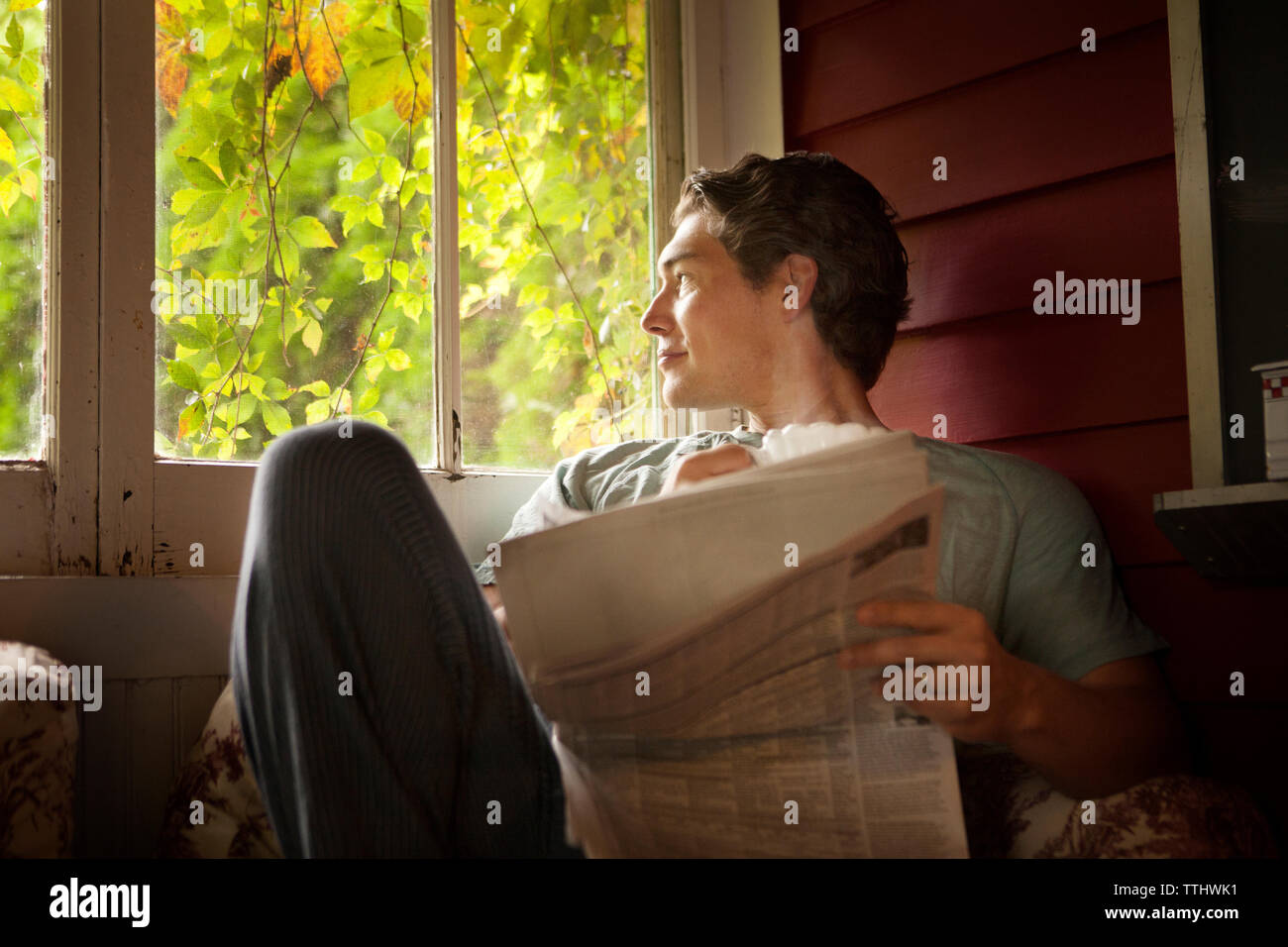 Man looking away while sitting by window at home Stock Photo - Alamy