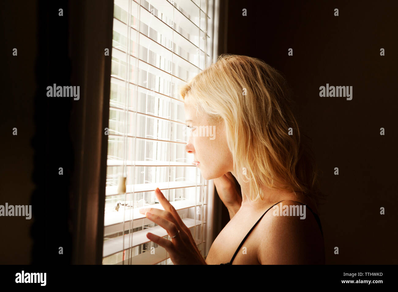 Side view of woman looking through window shutter at home Stock Photo ...