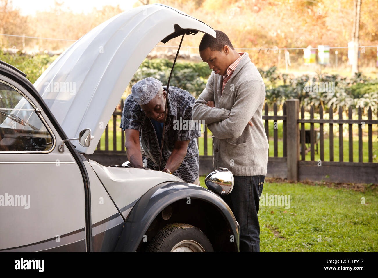 Senior man repairing car by son standing on grassy field Stock Photo ...