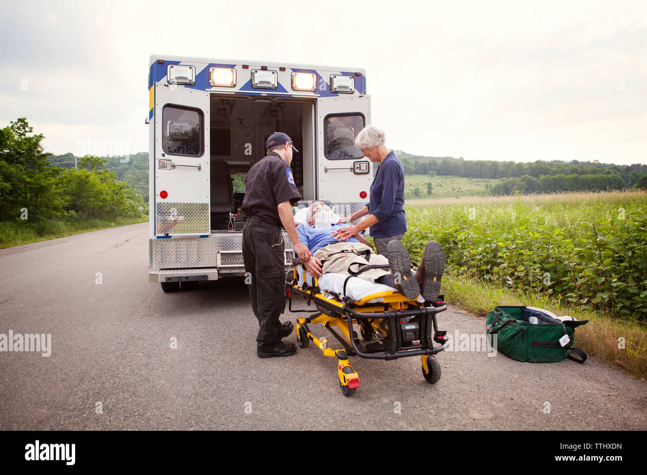 Patient lying on hospital gurney by paramedic and wife standing on road ...