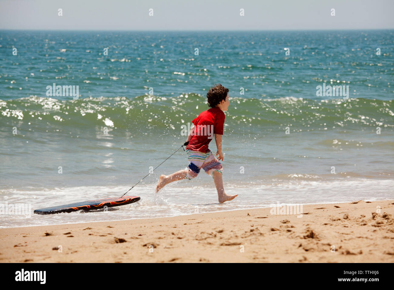 Boy running with surfboard on shore at beach Stock Photo - Alamy