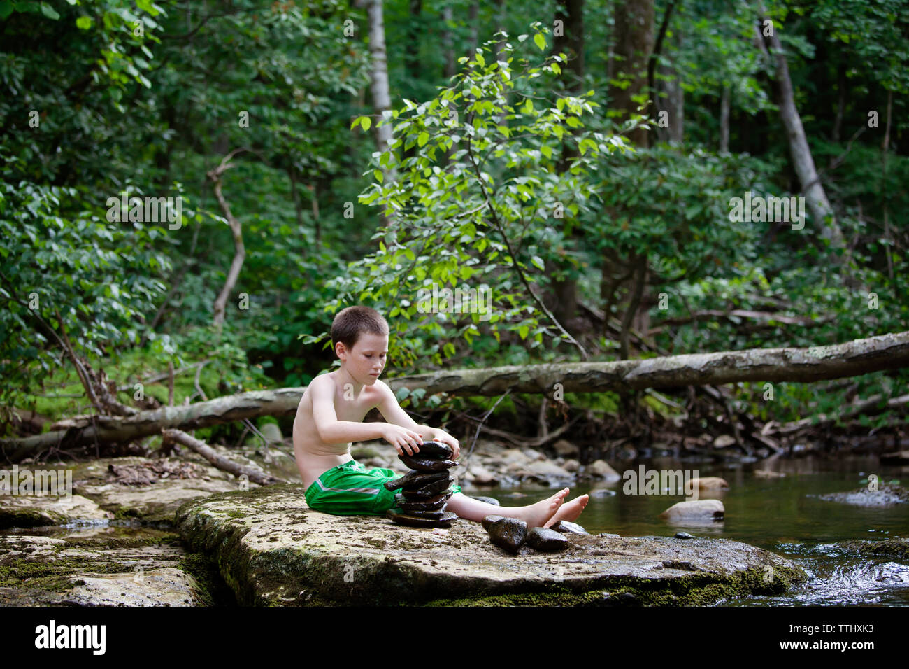 Boy arranging pebbles while sitting on rocks at lakeshore Stock Photo ...