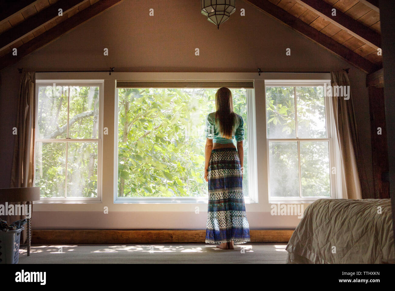 Rear view of woman standing by window at home Stock Photo - Alamy
