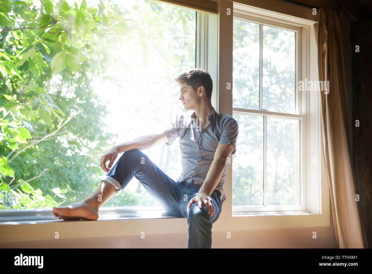 Thoughtful man sitting on window at home Stock Photo - Alamy