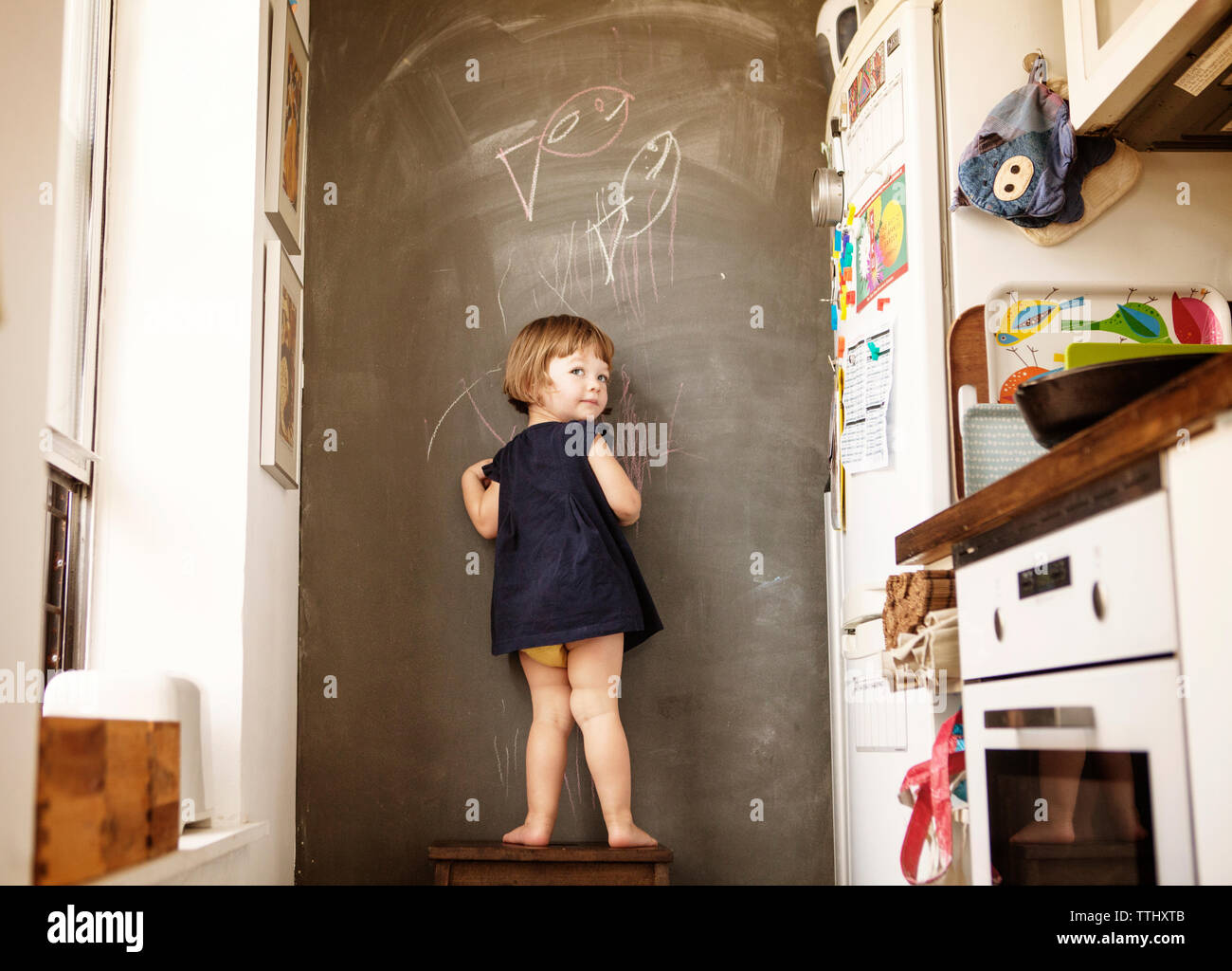 Rear view of girl writing on wall while standing on stool at home Stock ...