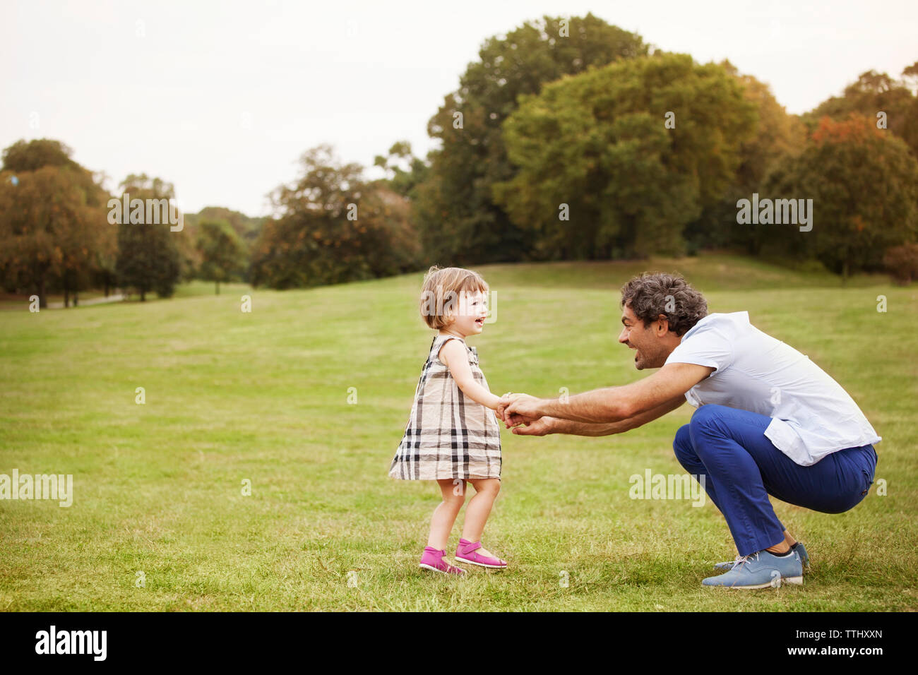 Side view of father crouching while holding daughter hands at park ...
