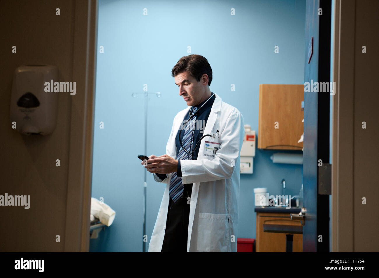 Doctor using mobile phone while standing in hospital Stock Photo - Alamy