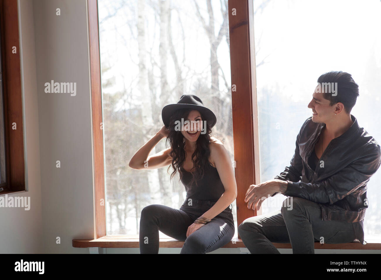 Cheerful couple sitting on window sill at home Stock Photo - Alamy