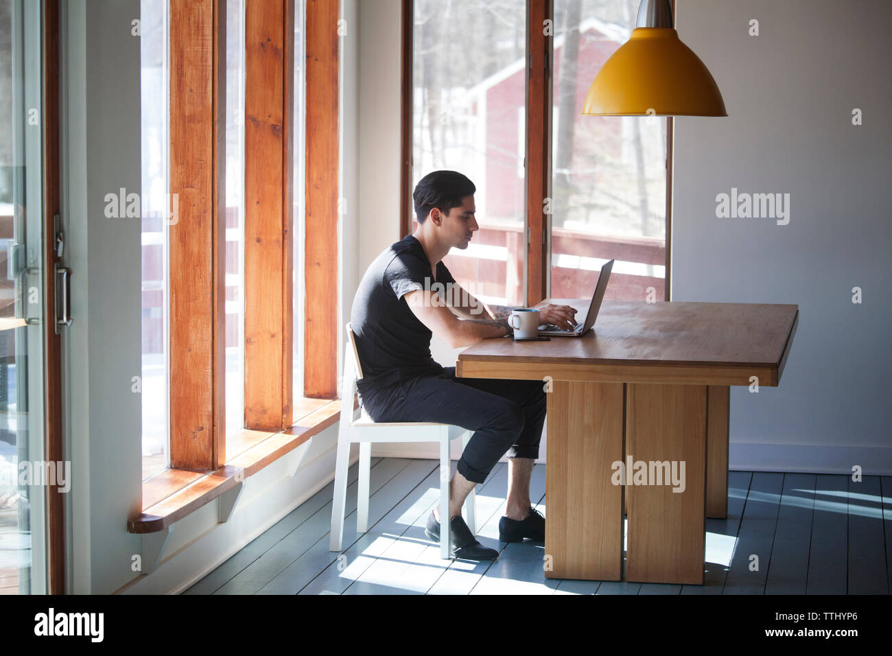 Side view of man using laptop computer while sitting on chair by table ...
