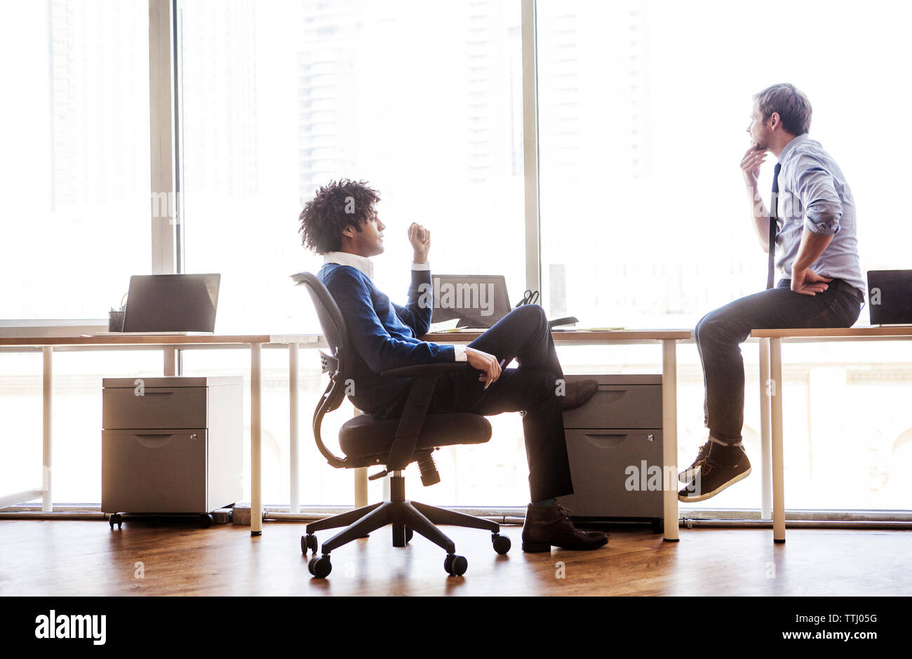 businessman looking through window while coworker sitting on chair at ...