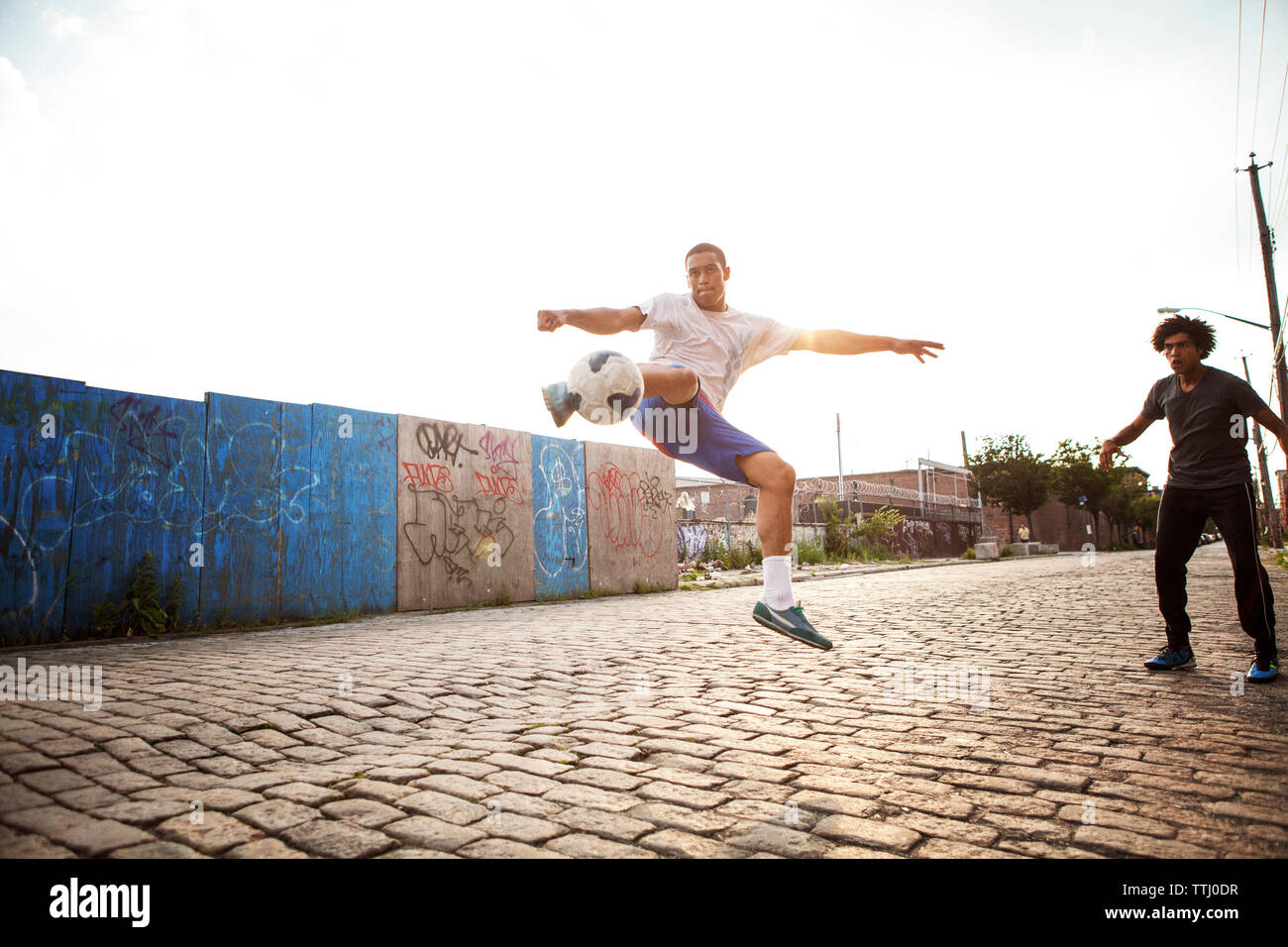 Man kicking soccer ball while friend looking at street Stock Photo - Alamy