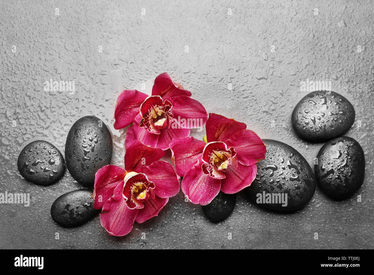 Spa stones and red orchid on grey background Stock Photo - Alamy