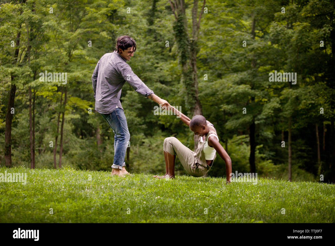 Man helping woman getting up from grassy field Stock Photo - Alamy