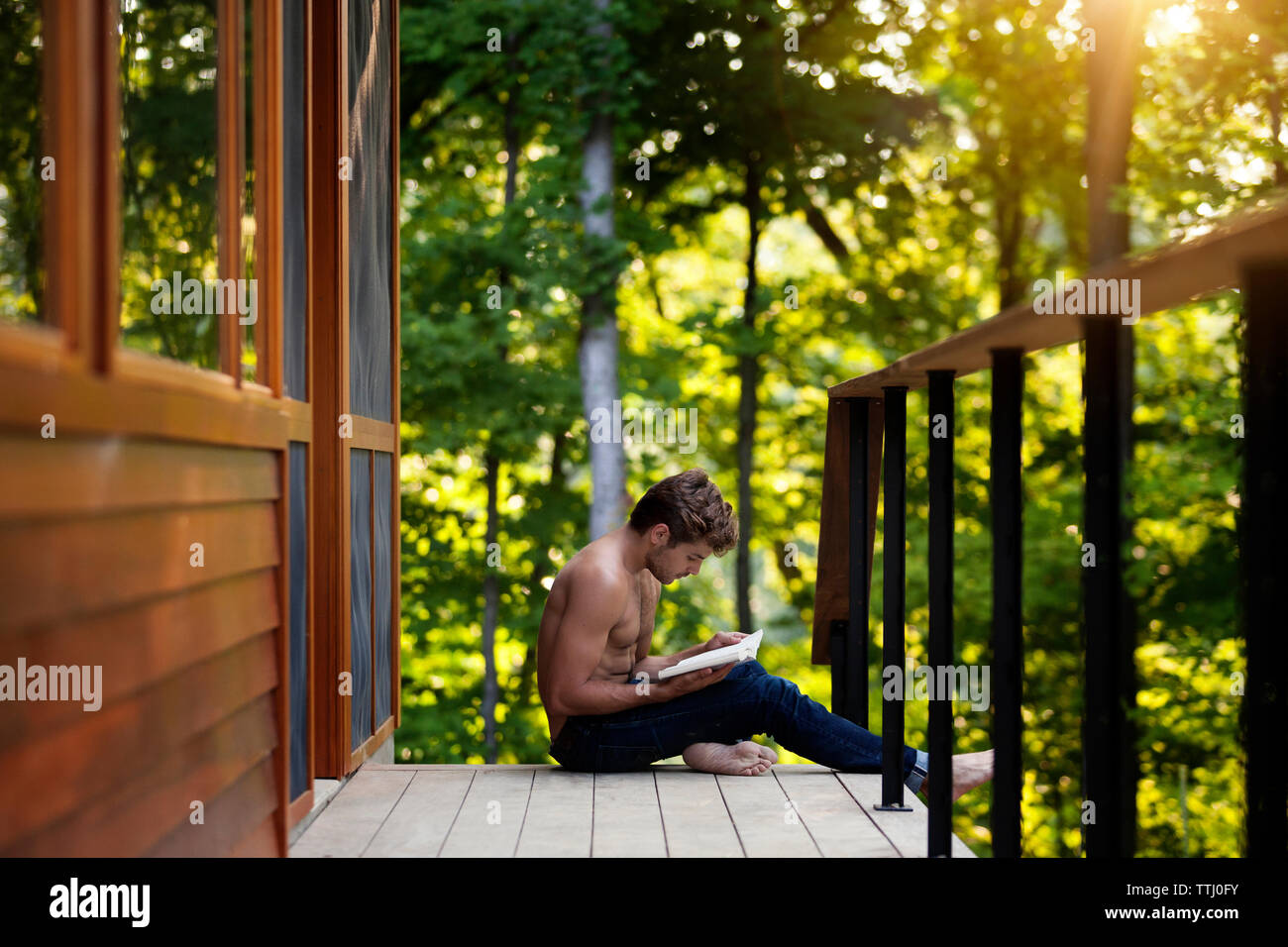 Boy reading book while sitting by railing in balcony Stock Photo - Alamy