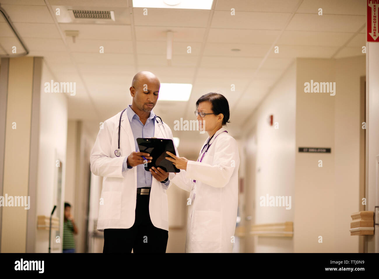 Female doctor showing reports to male doctor while standing in hospital ...