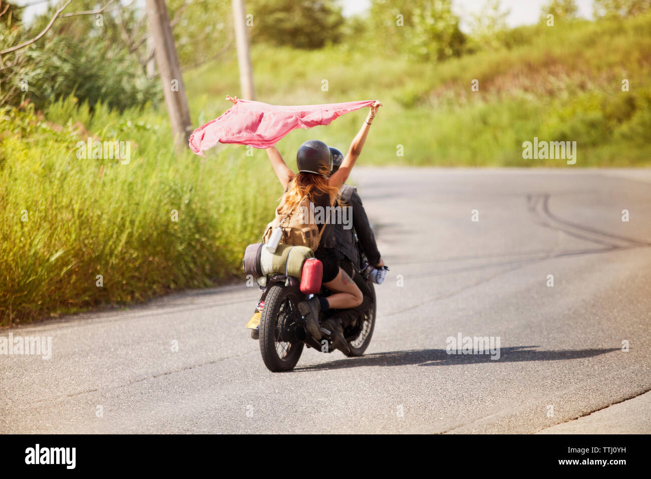 Woman holding aloft scarf while sitting on motorcycle with man Stock ...