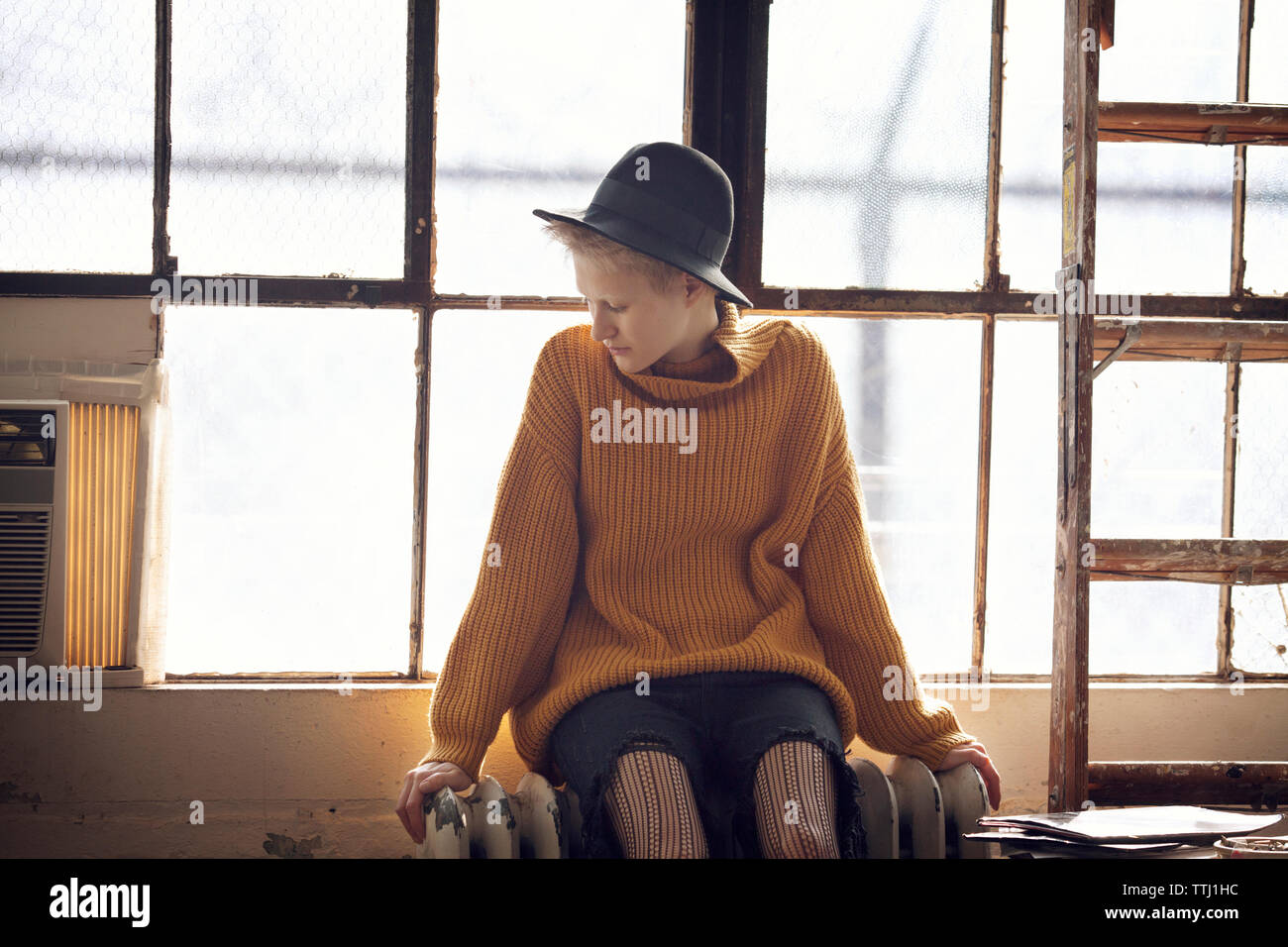 Woman looking down while sitting on radiator by window at home Stock ...