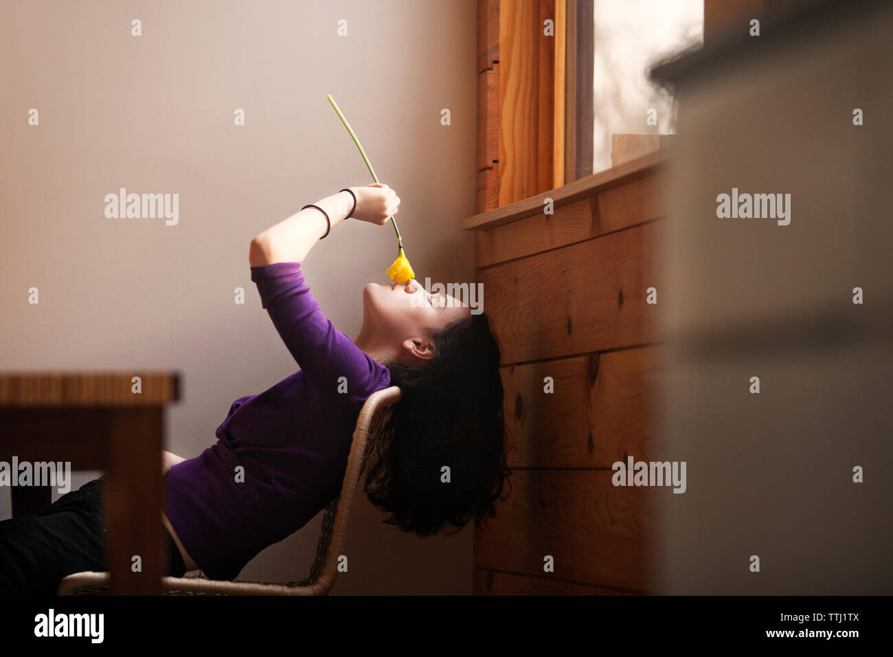 Side view of teenage girl smelling flower while sitting on chair at ...