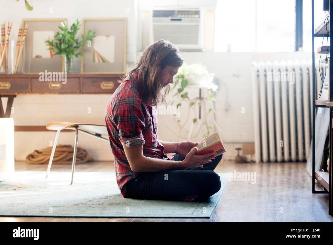Side view of man reading book while sitting at home Stock Photo - Alamy