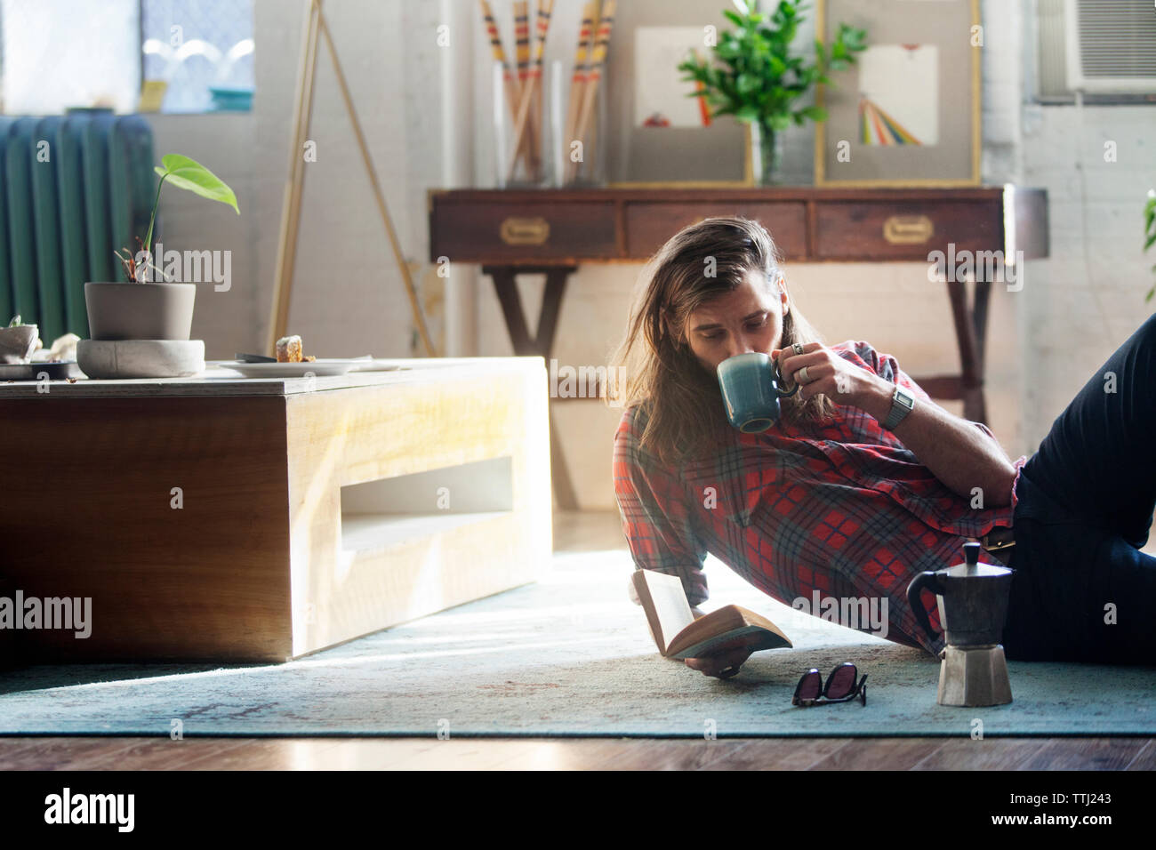 Man drinking coffee while reading book at home Stock Photo - Alamy