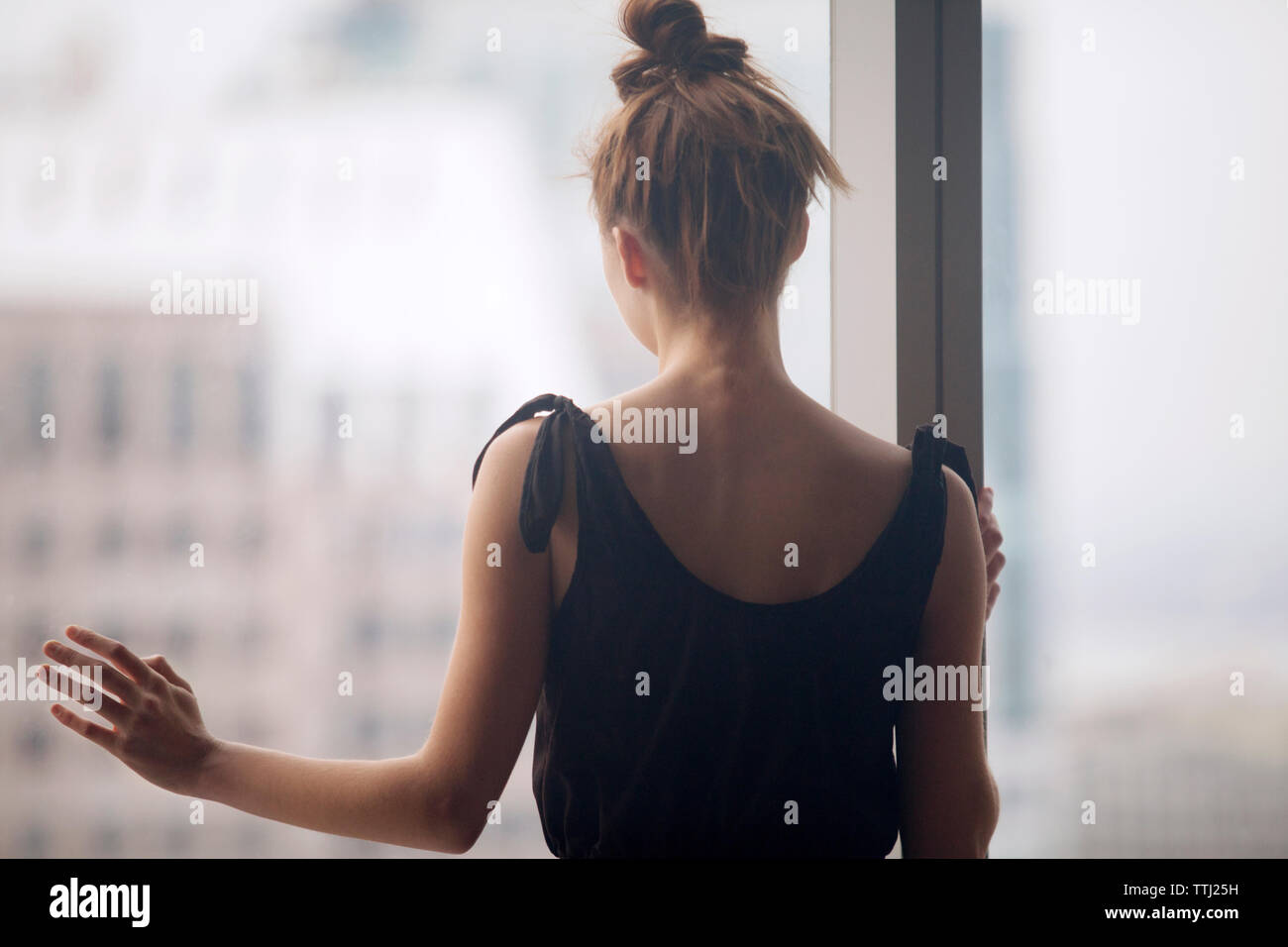 Rear view of woman standing by window Stock Photo - Alamy