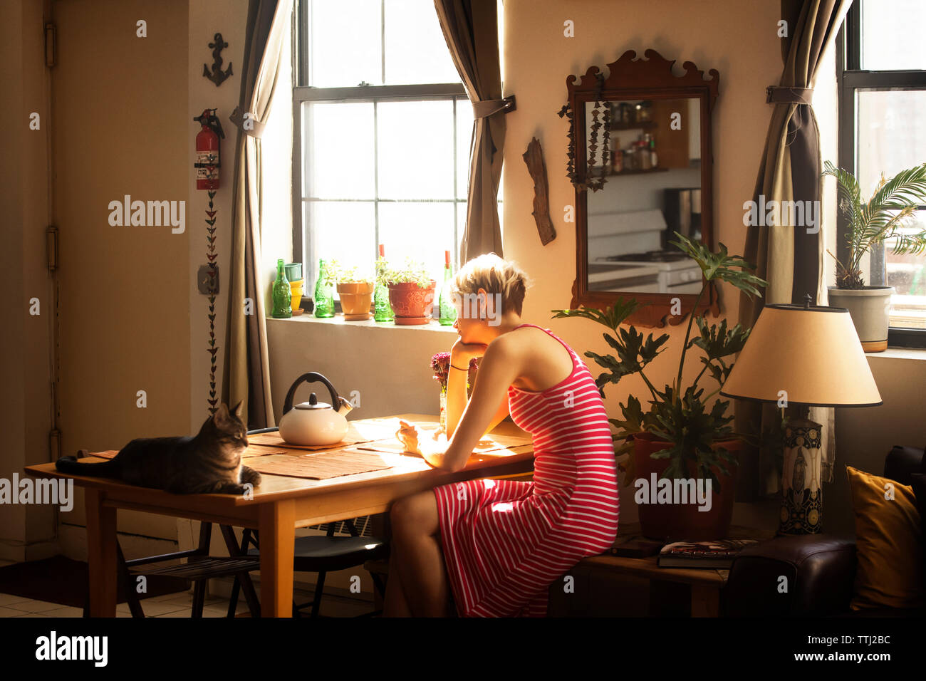 Side view of woman sitting by table at home Stock Photo - Alamy
