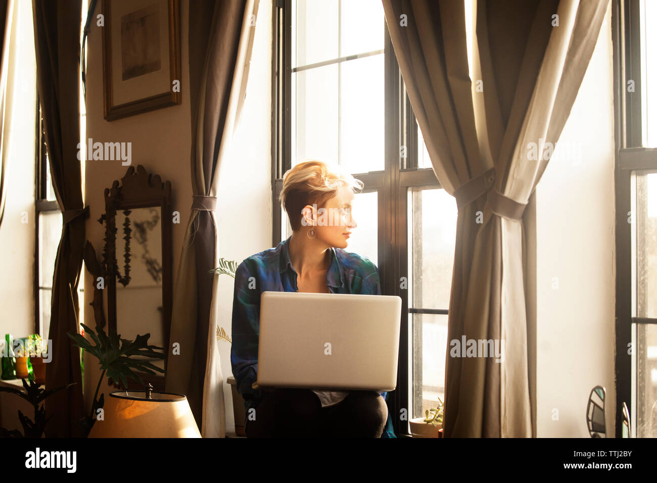Woman with laptop computer sitting on window sill at home Stock Photo ...
