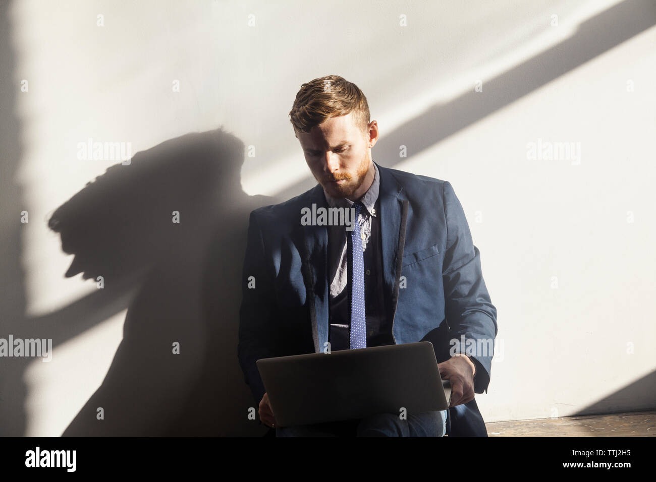 Man using laptop computer while sitting against wall at home Stock ...
