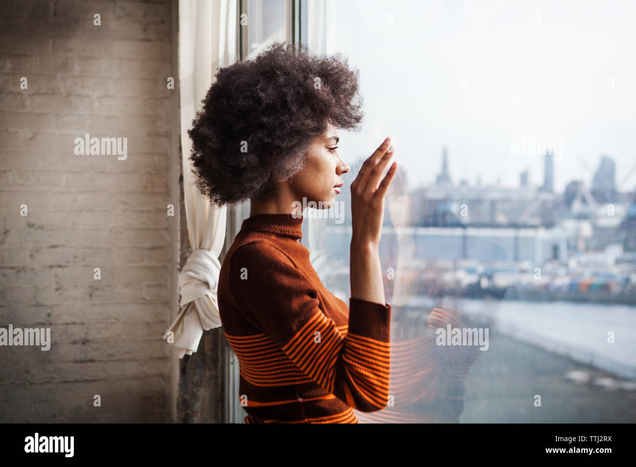 side view of woman looking though window at home Stock Photo - Alamy