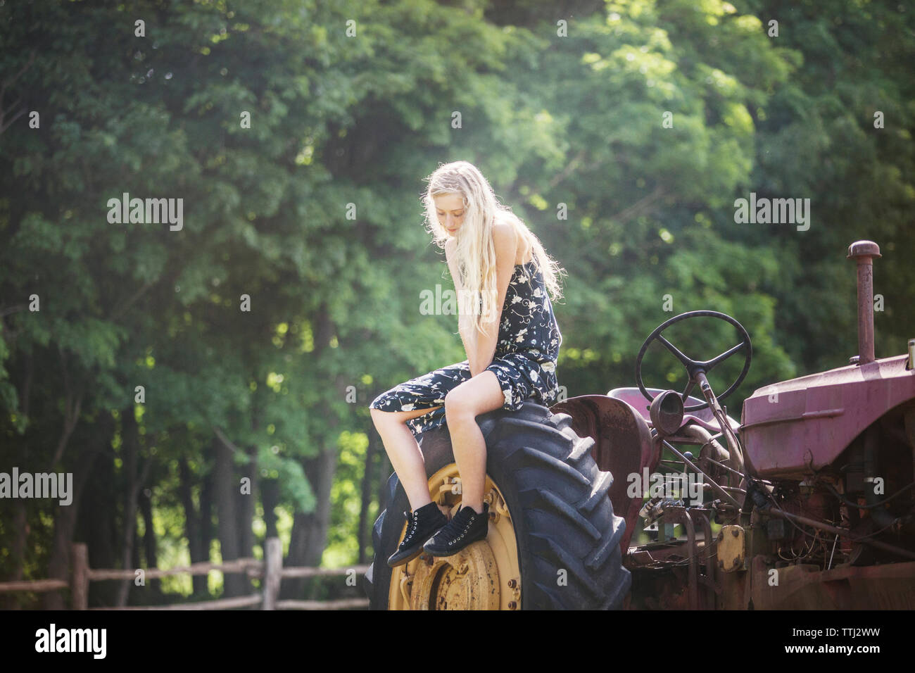 Woman looking down while sitting on tractor tire Stock Photo - Alamy