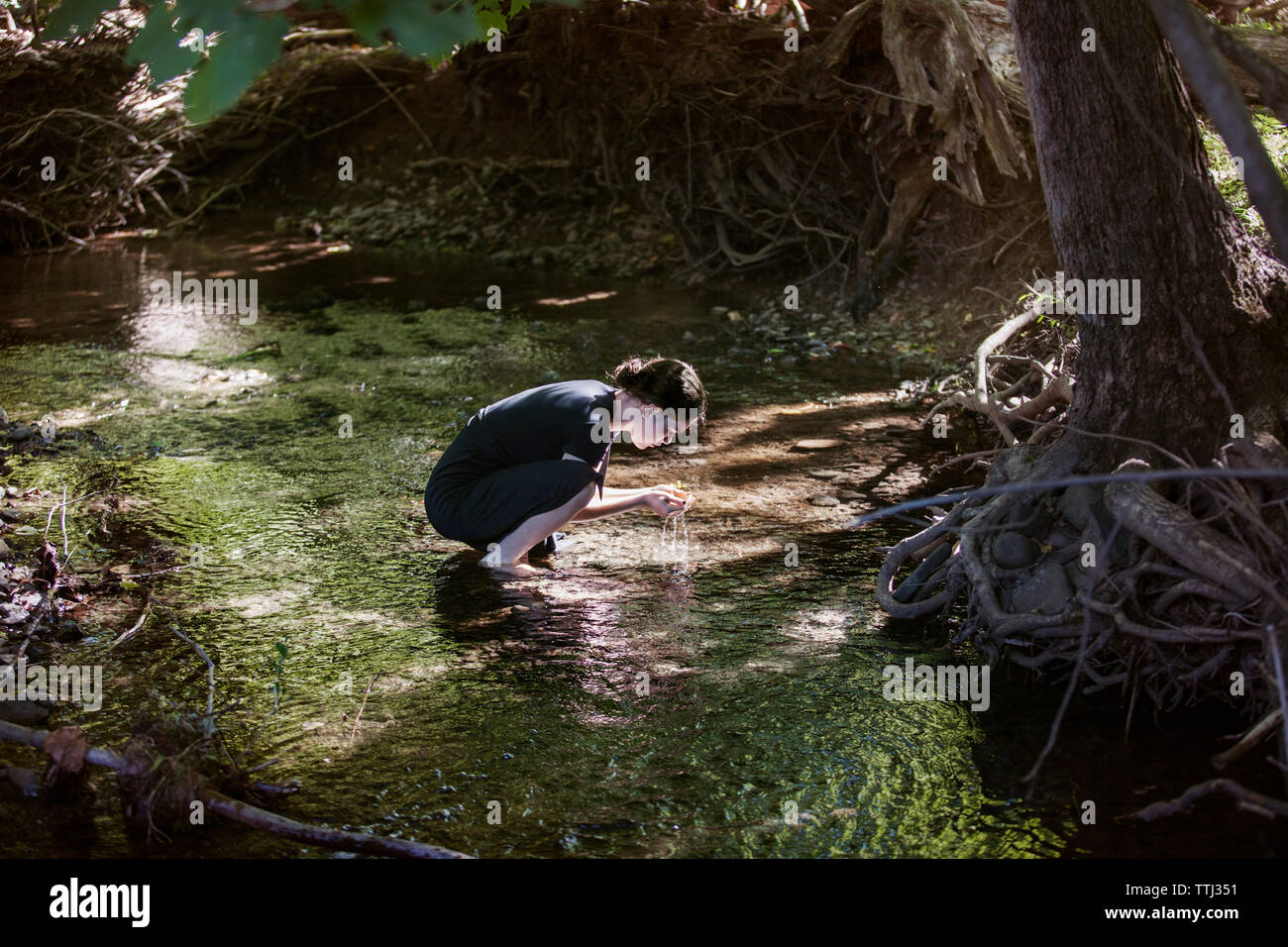 Side view of teenage girl holding water while crouching in stream Stock ...
