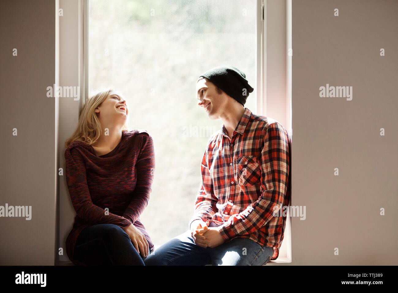 Cheerful couple talking while sitting on window sill Stock Photo - Alamy