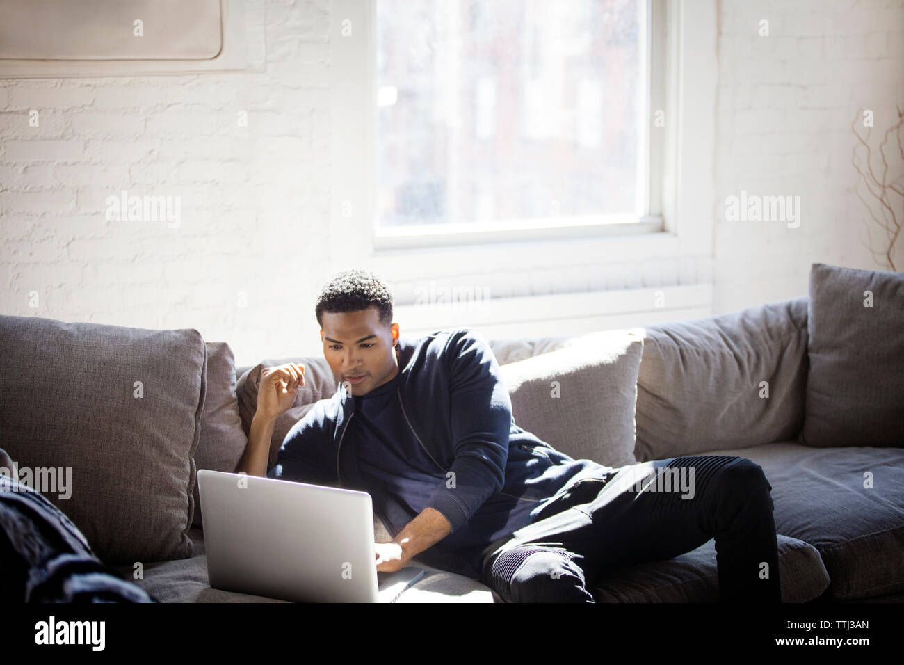 Man using laptop while sitting on sofa at home Stock Photo - Alamy