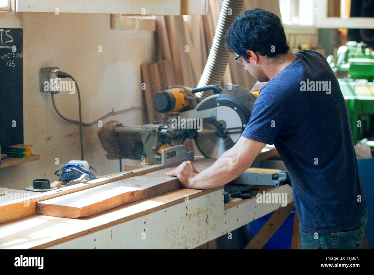 Side view of male carpenter cutting wooden plank with electric saw ...