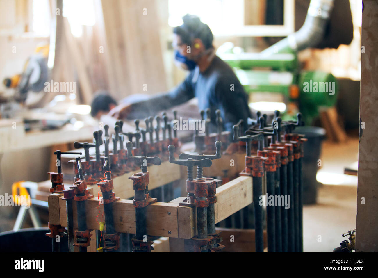 Side view of male carpenter in workshop with machinery in foreground ...