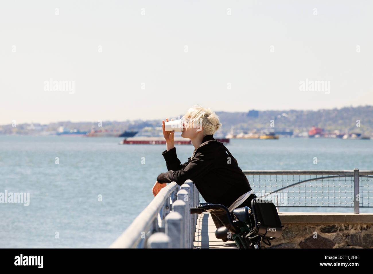 Woman drinking coffee while leaning on railing at observation point by ...