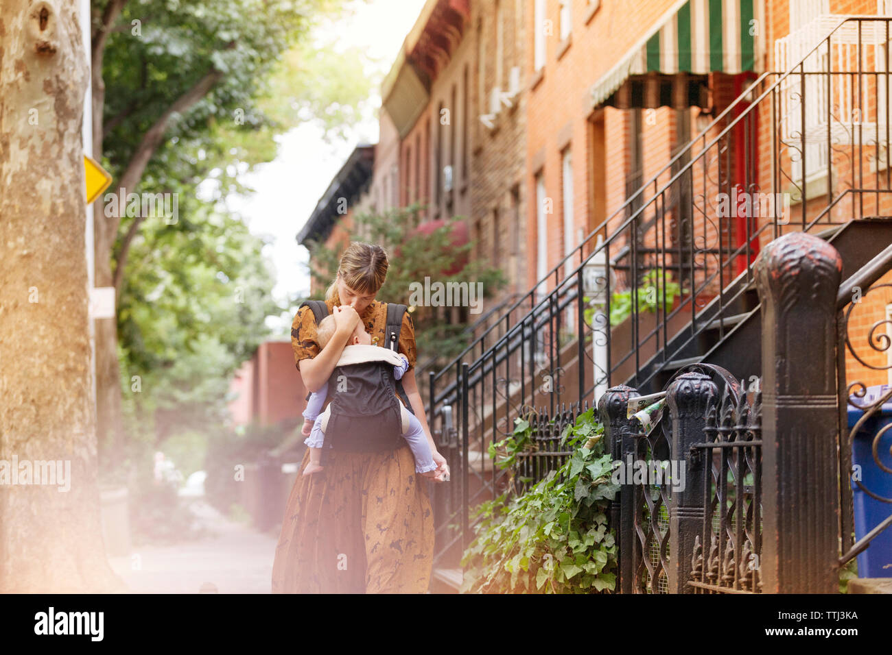 Woman carrying baby while walking on sidewalk Stock Photo - Alamy