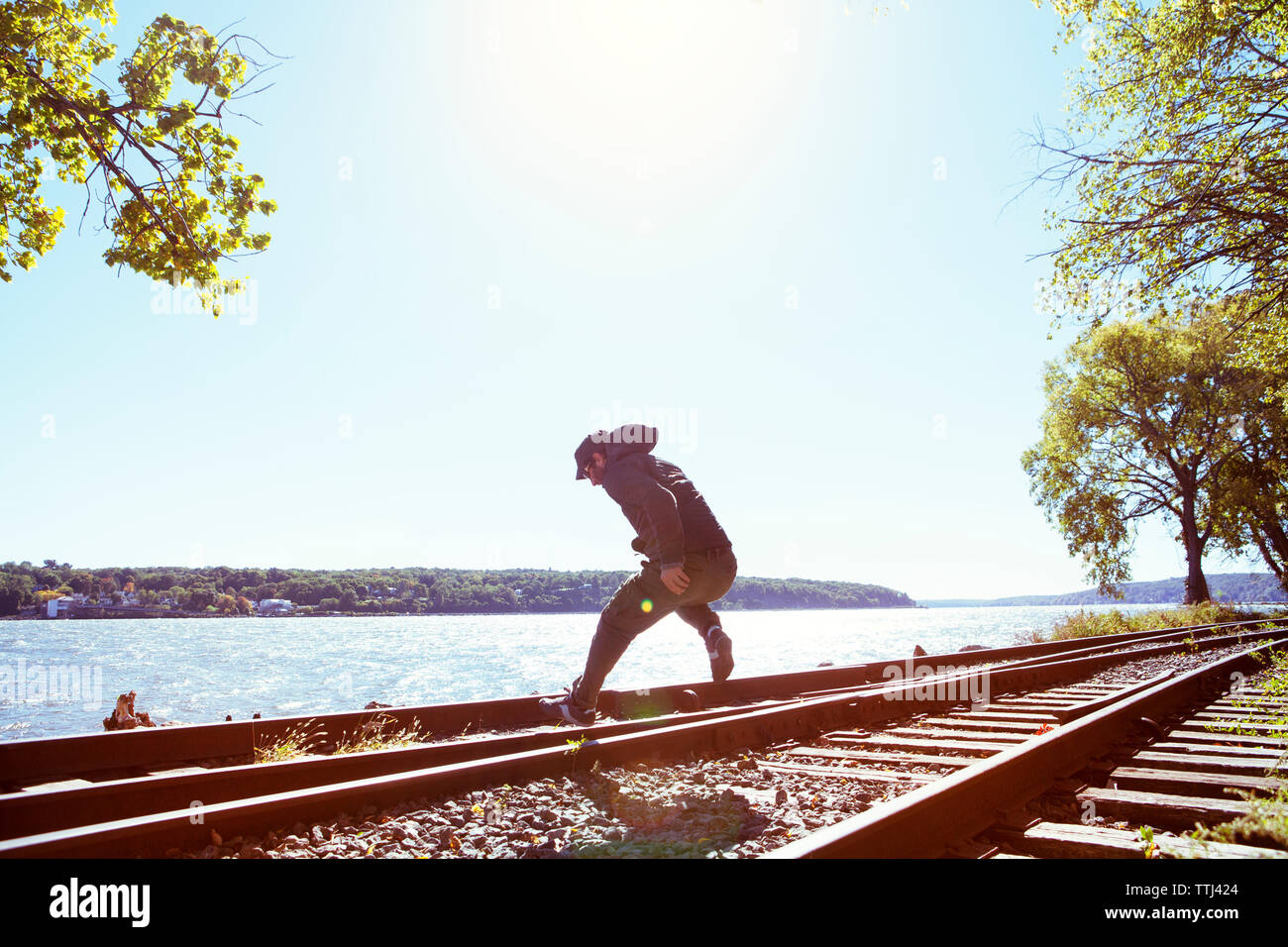 Man jumping on railroad tracks by river against clear sky Stock Photo ...
