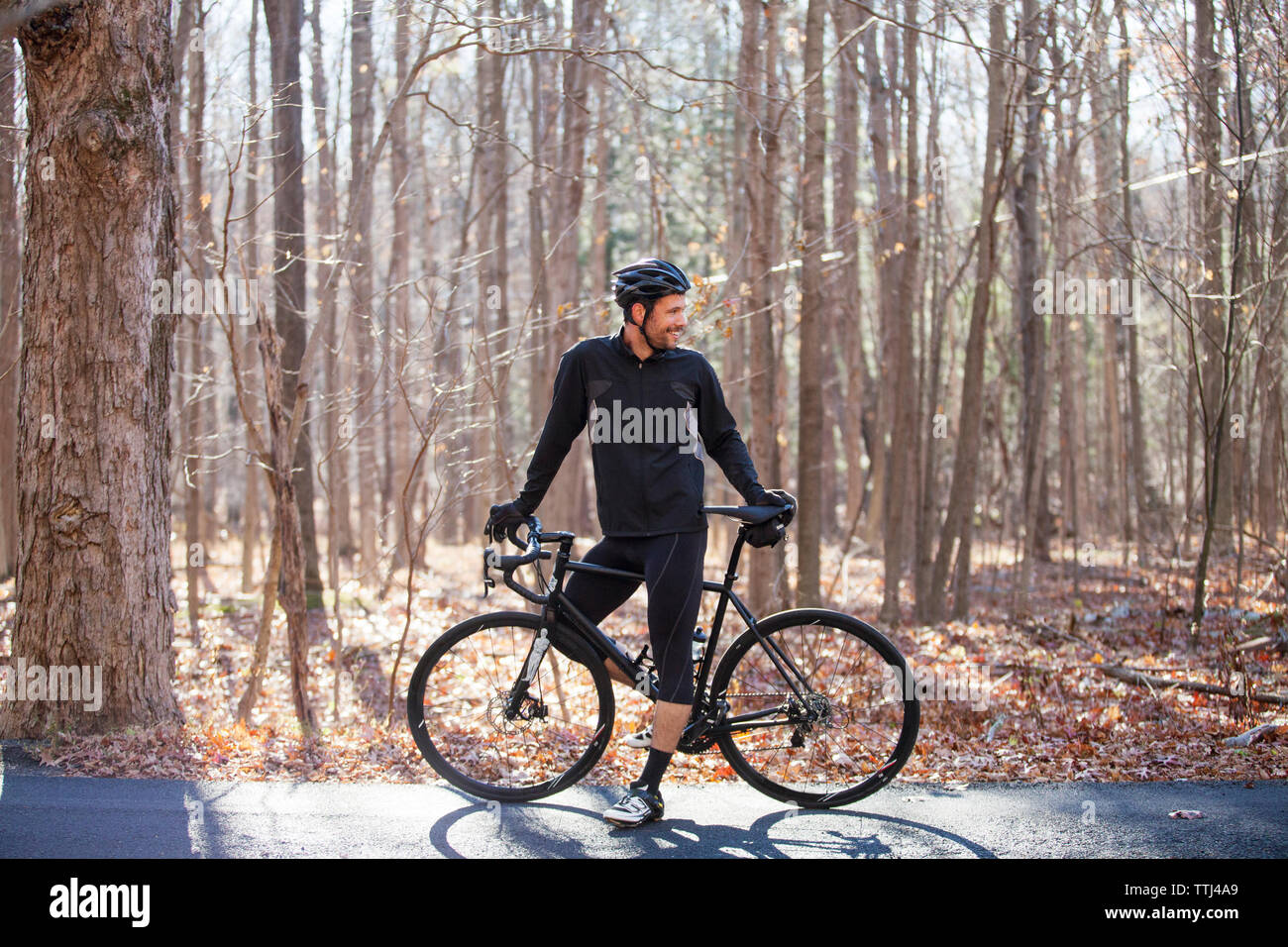 Cyclist standing by bicycle on road at forest Stock Photo - Alamy