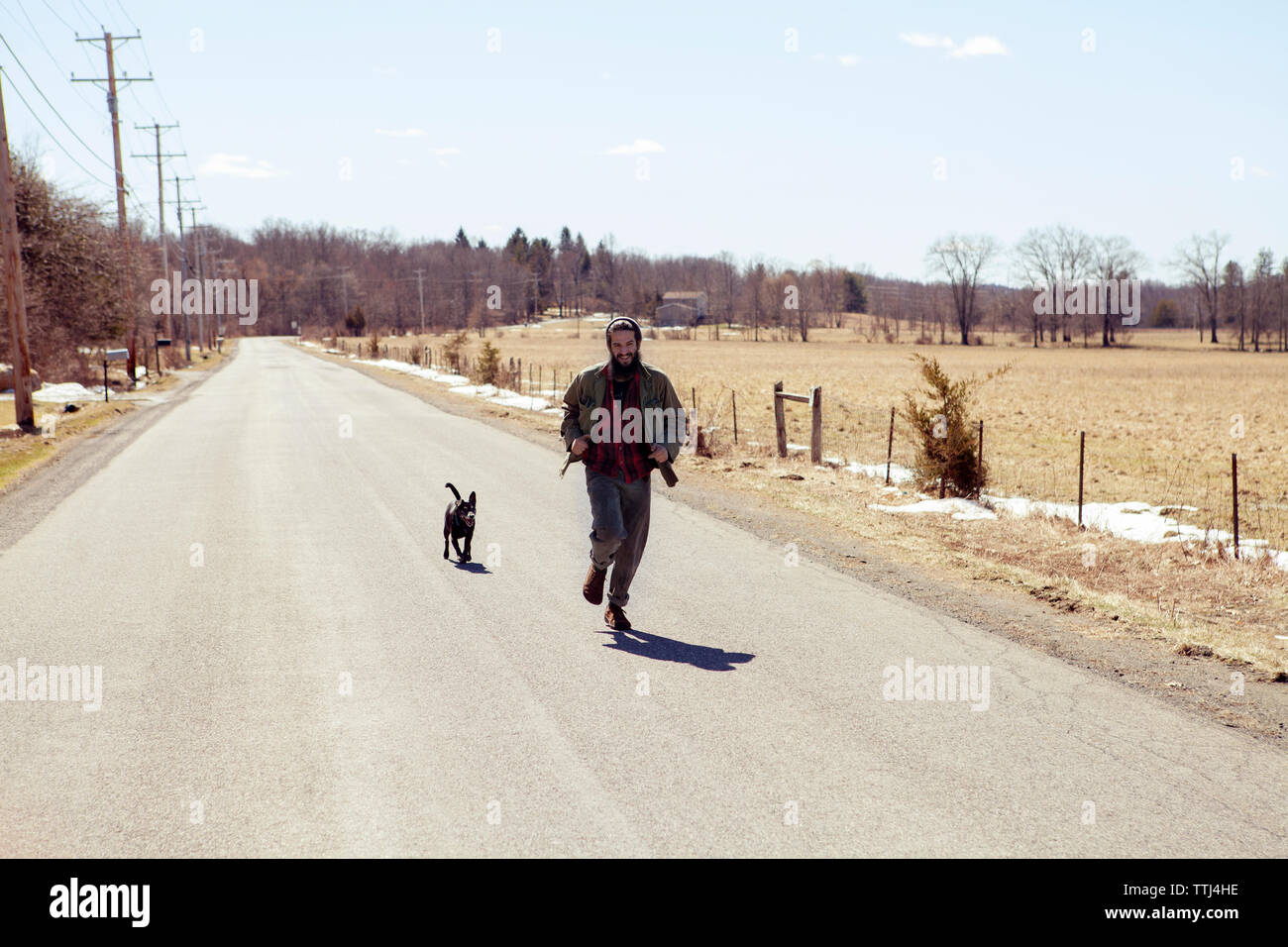 Full length of man and dog running on country road during vacation ...