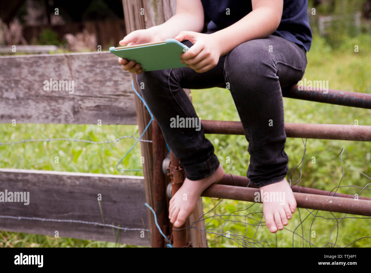 Low section of boy using tablet computer sitting on gate Stock Photo ...