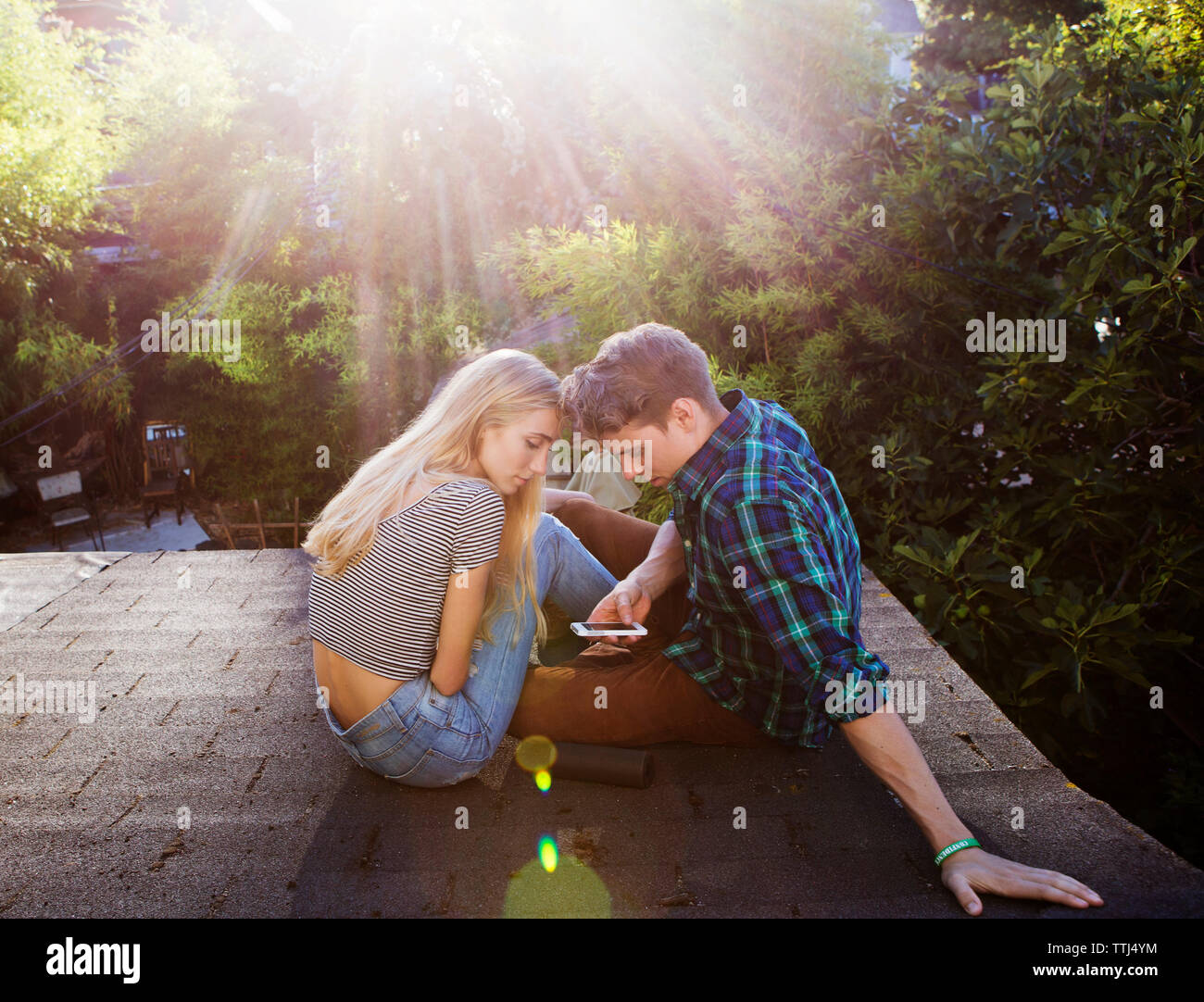 Couple using mobile phone while sitting on roof Stock Photo - Alamy