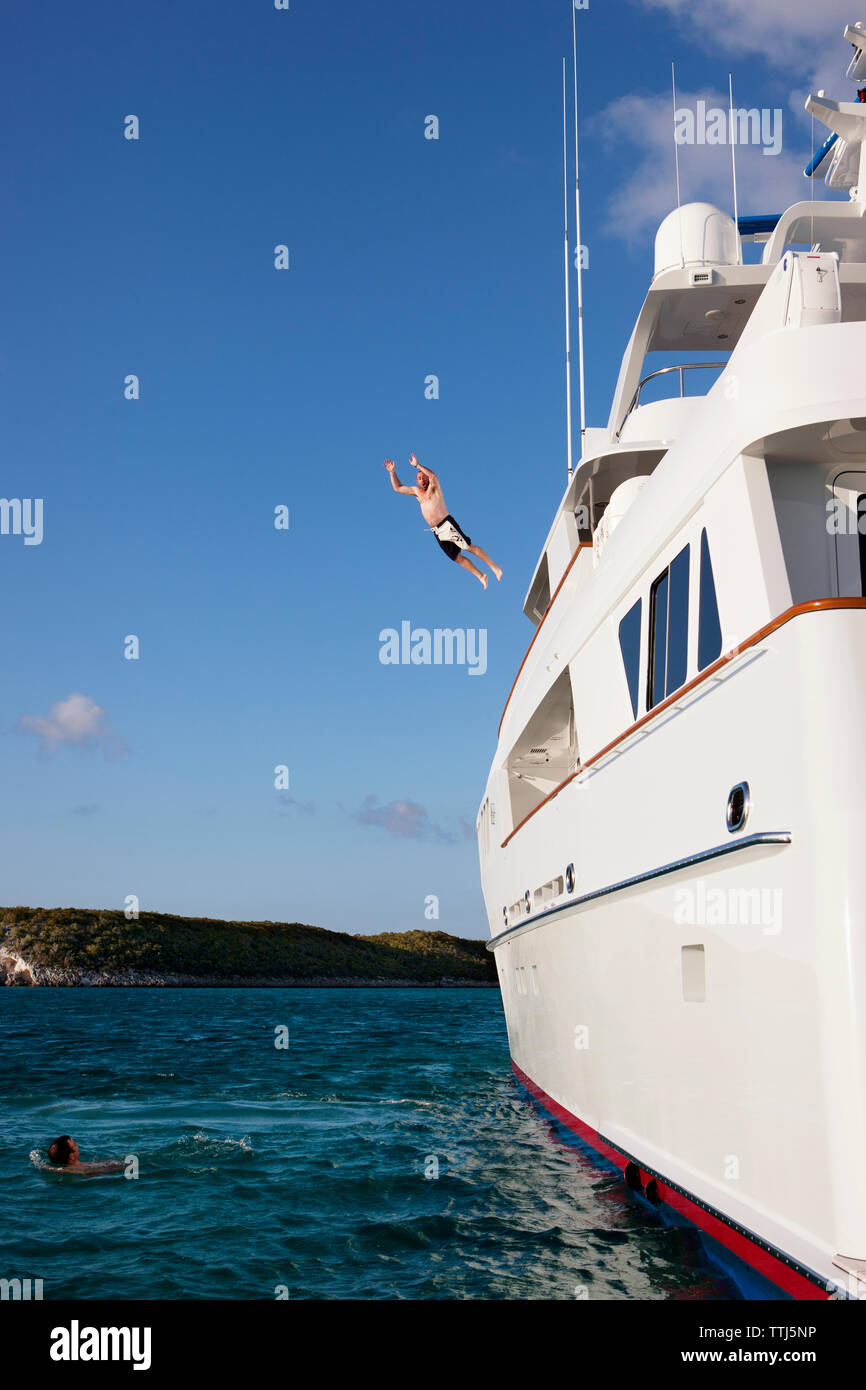 Man jumping from yacht while friend swimming in sea Stock Photo - Alamy