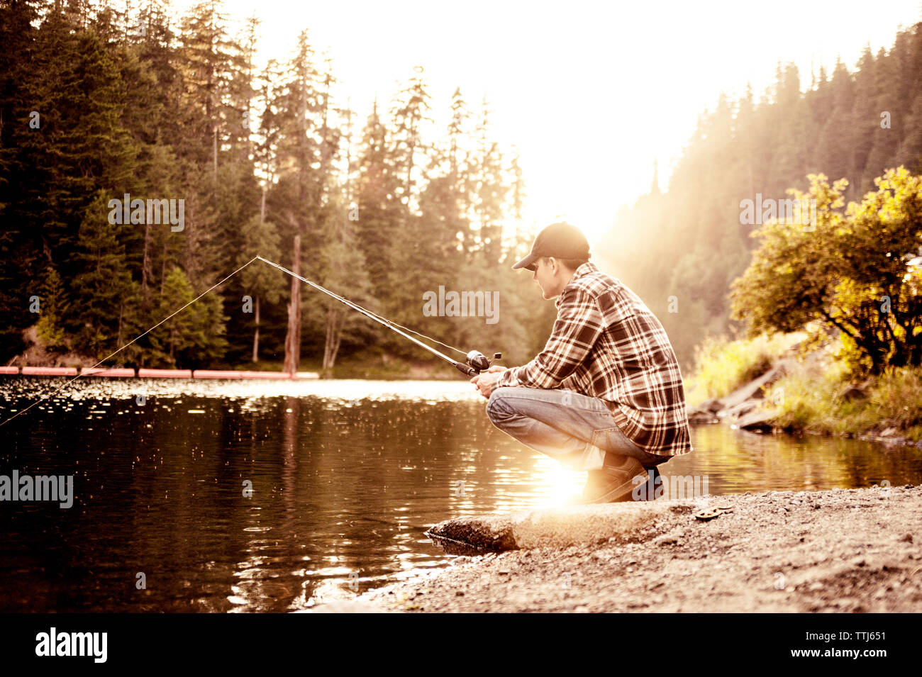 Side view of man fishing in lake at forest Stock Photo - Alamy