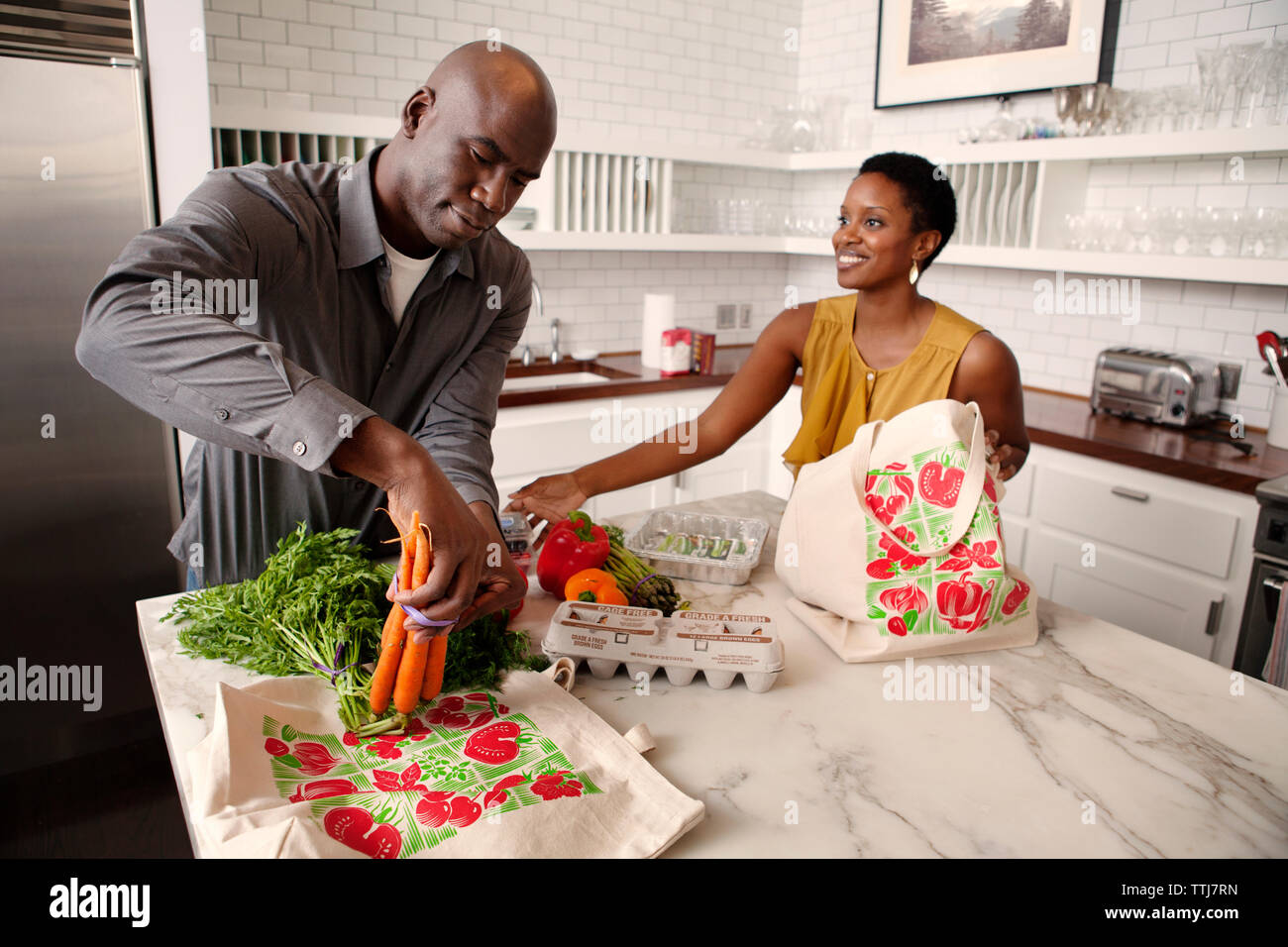 Woman looking at husband putting vegetables on kitchen island Stock ...