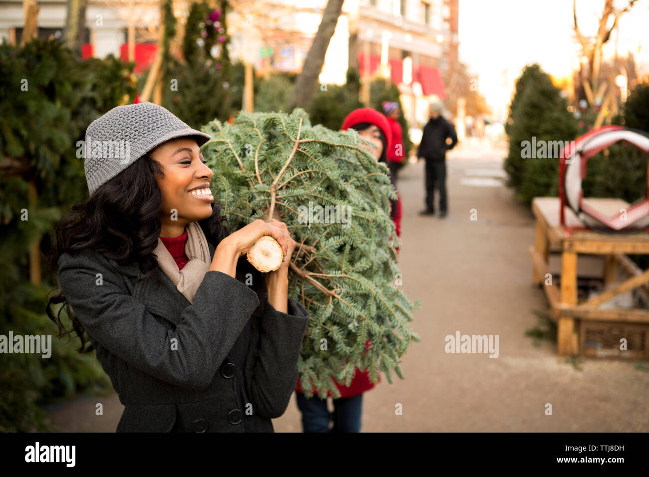 Happy woman carrying christmas tree on shoulder in market Stock Photo ...