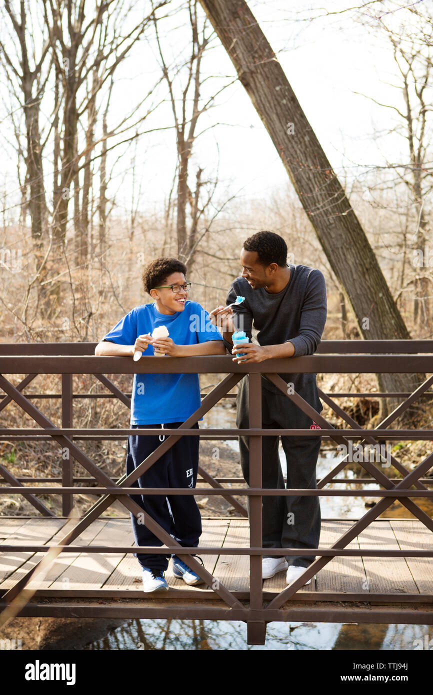 Happy father and son eating ice slush while standing on footbridge ...